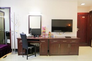 Quarto de hotel com uma escrivaninha de madeira, uma cadeira, uma TV de tela plana na parede, um armário e uma porta.