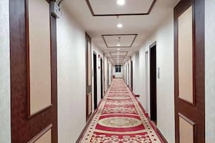 Corredor de hotel com carpete estampado, portas de madeira e teto com iluminação embutida.