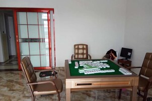 Quarto com mesa de bilhar verde, quatro cadeiras, televisão e porta com painéis de vidro jateado.