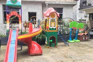 Um parquinho com um escorrega vermelho, uma estrutura de escalada e uma torre verde com um relógio.