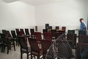 Uma sala de conferências com fileiras de cadeiras, um púlpito e um ventilador.