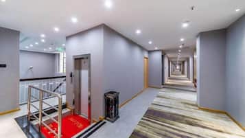 Corredor de hotel com tapete vermelho, corrimão de metal e piso coberto por carpete.