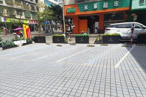 Área externa pavimentada com jardineiras e fachada de loja.