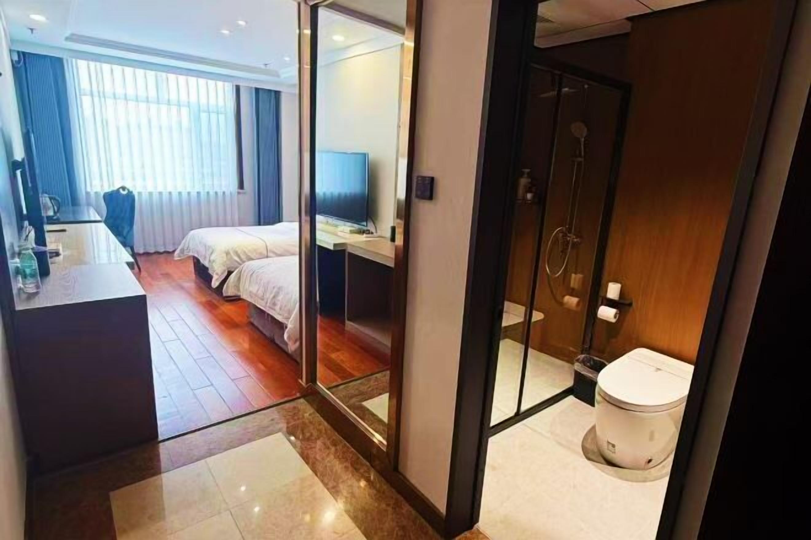 Quarto de hotel com cama, escrivaninha, chuveiro e vaso sanitário.
