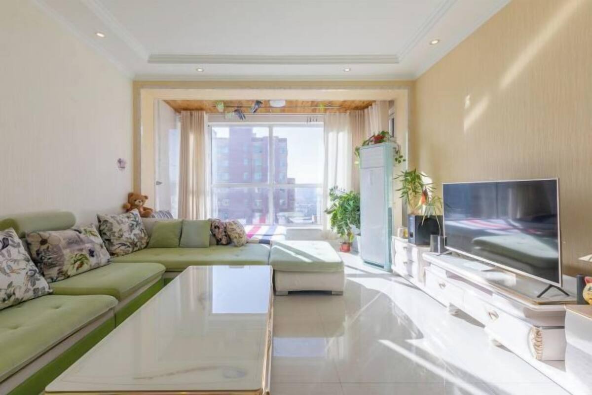 Uma sala de estar moderna com sofá, mesa de centro, televisão e vista para prédios.