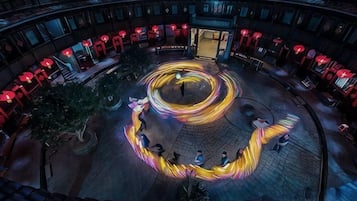 Área de estar circular com uma instalação de luz central, rodeada por lanternas vermelhas e mobiliário para área externa.