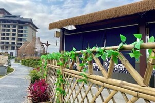 Cercado de bambu com vegetação, um caminho e um edifício com telhado de palha.