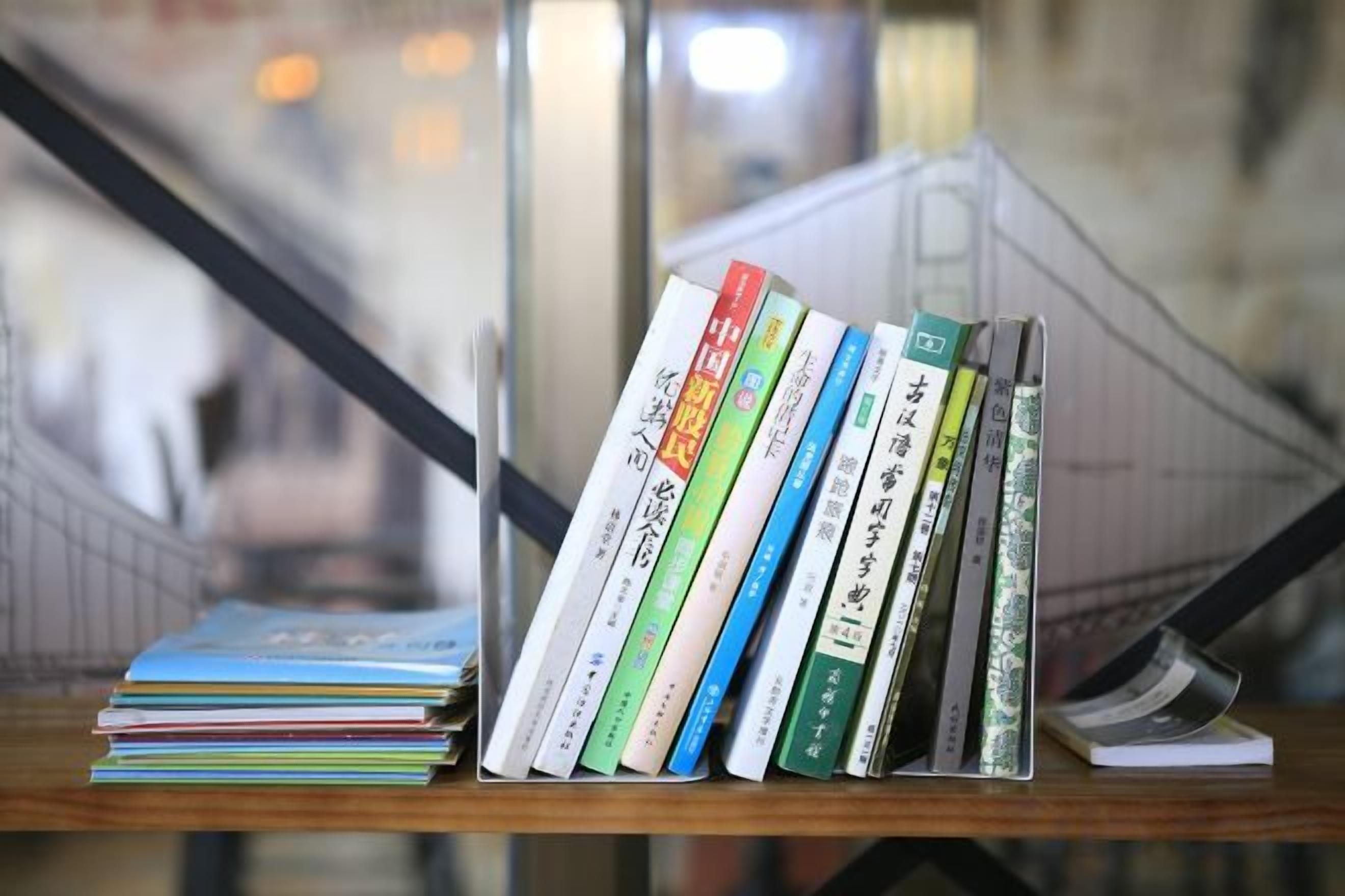 Uma pilha de livros sobre uma superfície de madeira, com uma vitrine de vidro ao fundo.