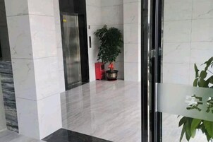 Um saguão com piso de mármore, um armário vermelho e uma planta em vaso.