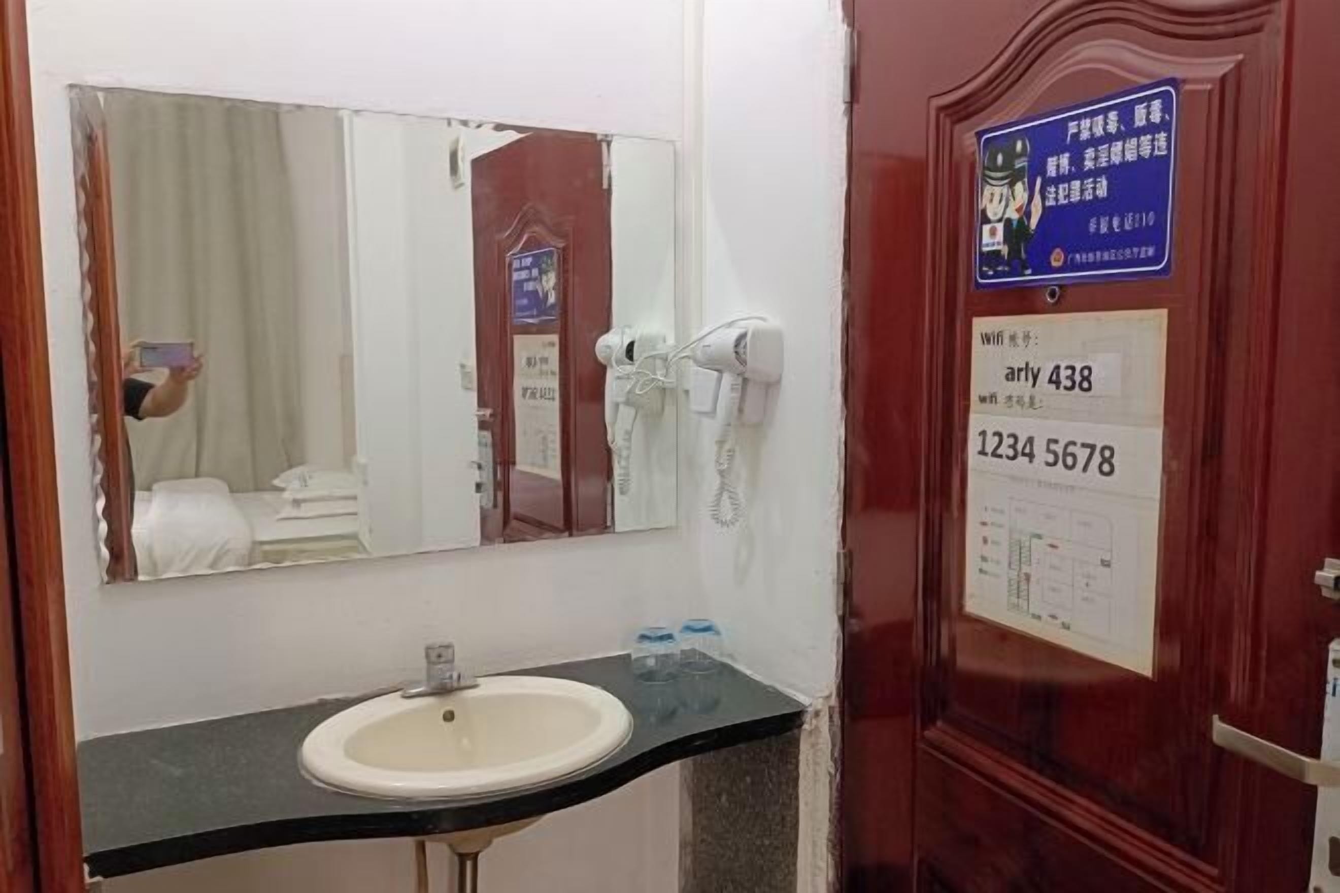 Casa de banho com lavatório, espelho e telefone fixado na parede. Duas garrafas de água estão no balcão.