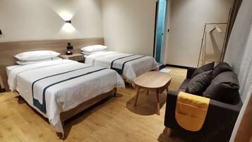 Quarto de hotel com duas camas de solteiro, um sofá, uma mesinha e um guarda-roupa.