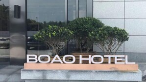 Placa do HOTEL BOAO com design moderno, exibindo claramente o nome do hotel e um reflexo da área circundante na fachada de vidro.