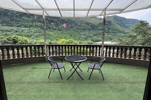Uma varanda com mesa e cadeiras, cercada por grades, com vista para uma paisagem verde exuberante.