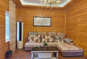 Um quarto aconchegante com paredes de madeira, um sofá com almofadas florais, uma mesinha e uma obra de arte emoldurada na parede.