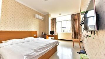 Quarto de hotel com cama, televisão, escrivaninha e cadeira, e janela com cortinas.
