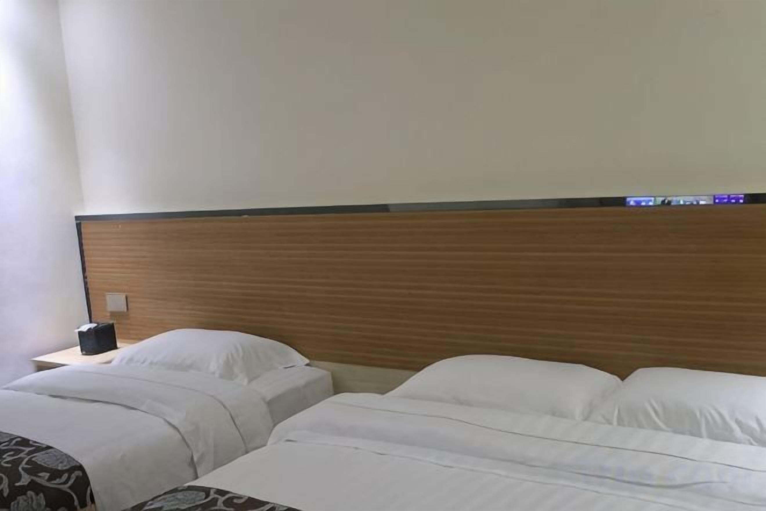 Quarto de hotel com duas camas, uma cabeceira de madeira e uma mesa de cabeceira com abajur.