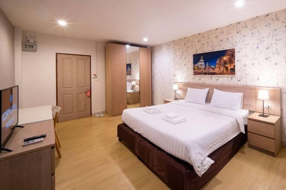 Quarto de hotel com uma cama grande, mesas de cabeceira com luminárias, uma televisão e um quadro na parede.