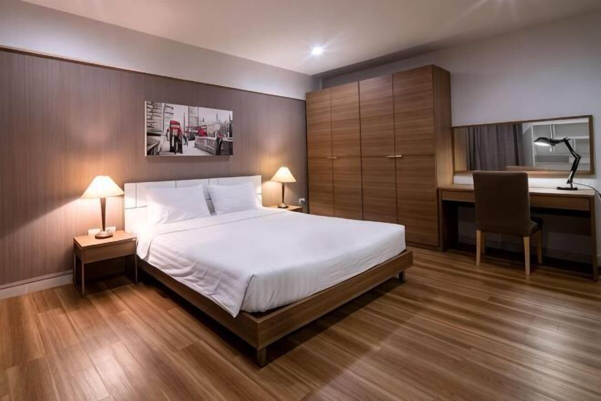 Um quarto com uma cama, mesas de cabeceira, escrivaninha e guarda-roupa.