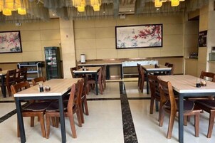 Interior de restaurante com várias mesas, cadeiras, balcão e obras de arte nas paredes.