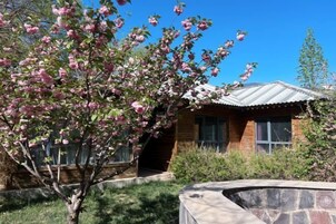 Uma casa com um alpendre de pedra, um deck de madeira e uma árvore com flores cor-de-rosa.
