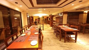 Restaurante com várias mesas preparadas para hóspedes, com um lustre central e piso estampado.