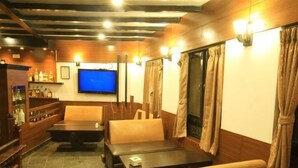Um espaço de bar acolhedor com mobiliário de madeira, uma televisão de tela plana e um balcão repleto de garrafas.