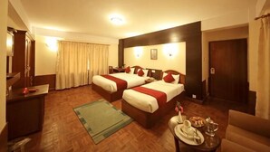 Quarto de hotel com duas camas, uma escrivaninha, uma cadeira, uma mesinha com bandeja e um sofá.