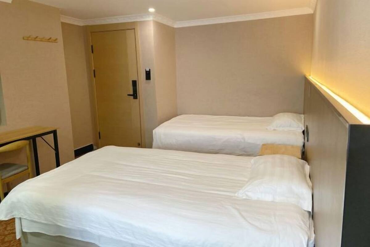 Quarto de hotel com duas camas, uma escrivaninha e uma porta.