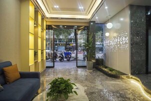 Um saguão de hotel com balcão de recepção, área de estar e entrada por porta de vidro.