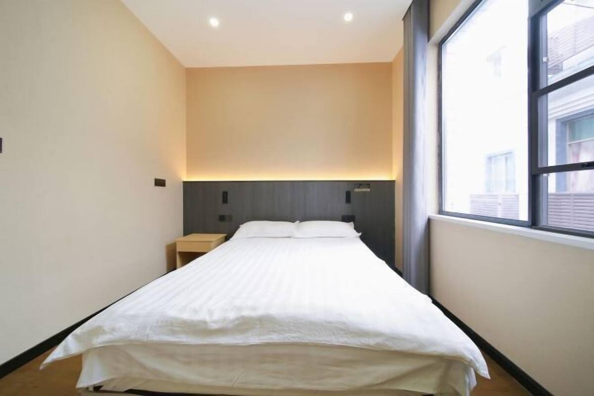 Quarto de hotel com uma cama de solteiro, mesa de cabeceira e uma janela grande com vista para o exterior.