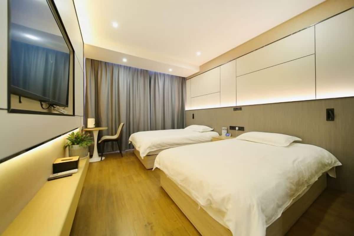 Quarto de hotel com duas camas, uma escrivaninha, uma cadeira, uma televisão e uma cortina.