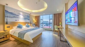 Quarto de hotel moderno com uma cama grande, vista para a cidade, televisão de tela plana e uma escrivaninha com cadeira.