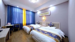 Quarto de hotel com duas camas, uma escrivaninha, uma cadeira, uma mesa com uma caneca rosa e uma luminária na parede.