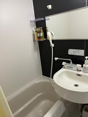 Casa de banho com lavatório branco, chuveiro manual e prateleira com artigos de higiene pessoal.