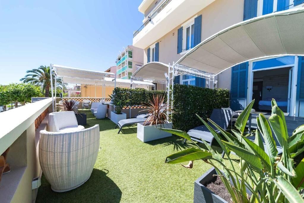 Terraço no telhado com grama sintética, mobiliário para área externa e vasos com plantas.