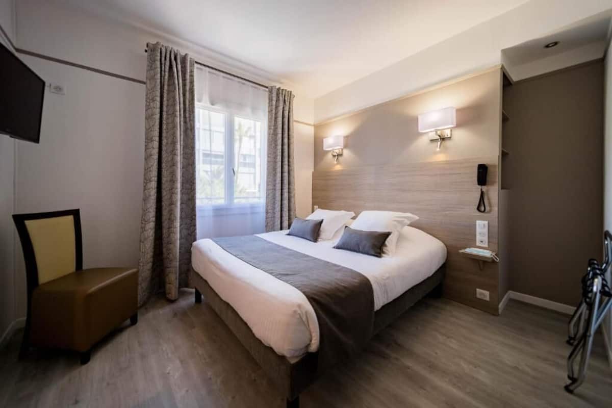 Quarto de hotel com cama, cadeira, televisão e porta.