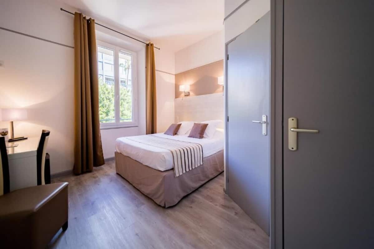 Quarto com cama, escrivaninha e janela com cortinas.