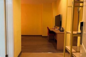 Um quarto com piso de madeira, uma escrivaninha com cadeira, uma televisão e uma estante.