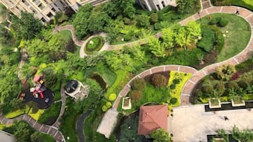 Vista aérea de um pátio ajardinado com caminhos, uma fonte central e vegetação ao redor.