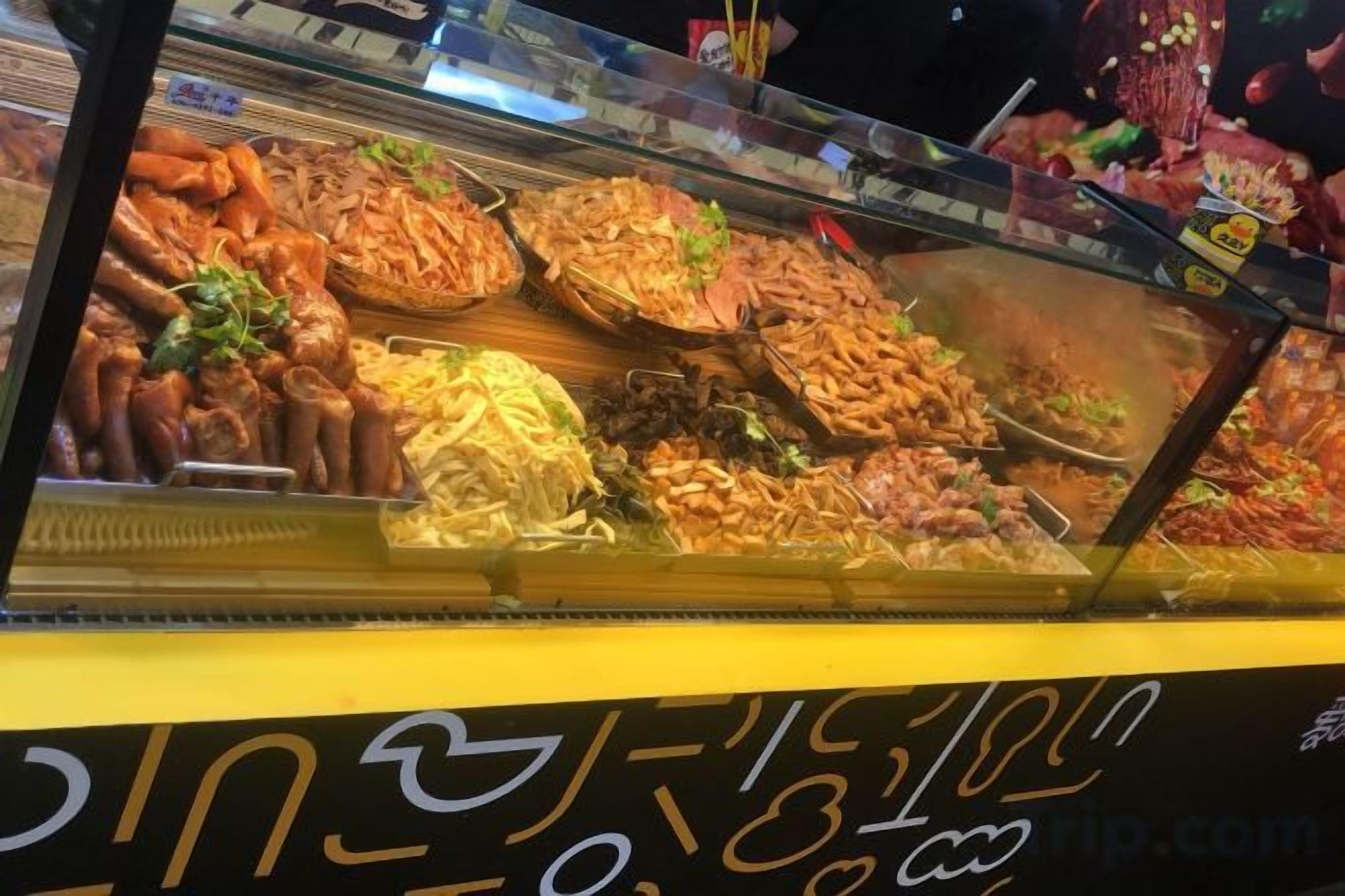 Vitrine de vidro com diversos alimentos, incluindo salsichas, carnes e legumes.