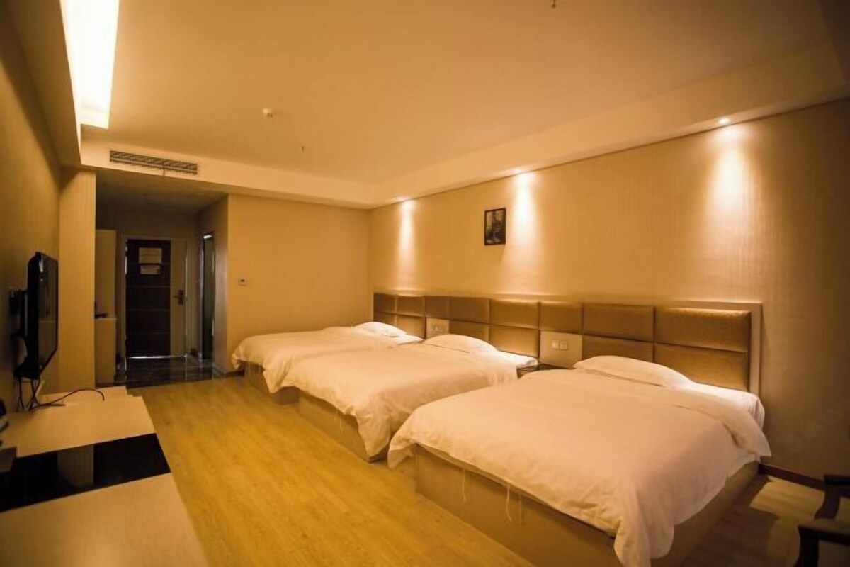 Quarto de hotel com duas camas, televisão e piso de madeira.