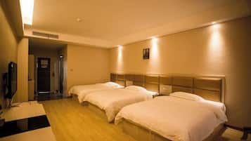 Quarto de hotel com duas camas, televisão e piso de madeira.