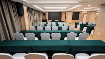 Uma sala de conferência com fileiras de mesas e cadeiras, uma tela de projetor e um palco.