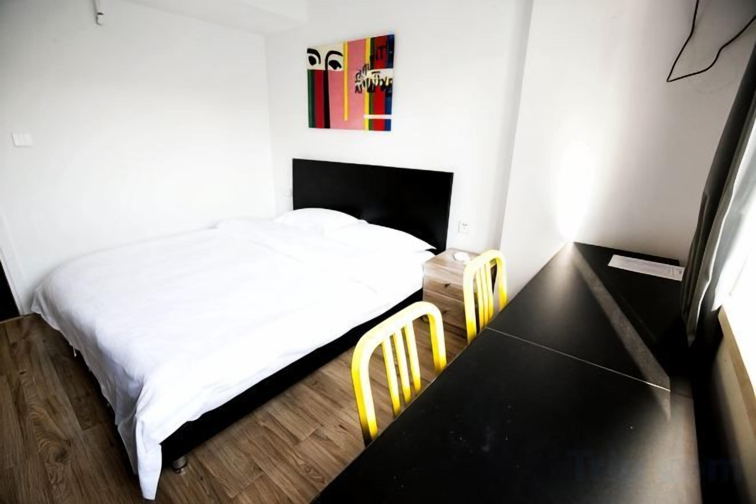 Quarto com cama, escrivaninha, cadeira e uma obra de arte na parede.
