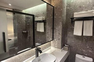 Uma casa de banho moderna com chuveiro separado por vidro, um espelho grande e uma pia branca.