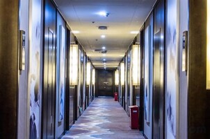 Corredor de hotel com portas em ambos os lados, carpete estampado e uma lixeira vermelha.