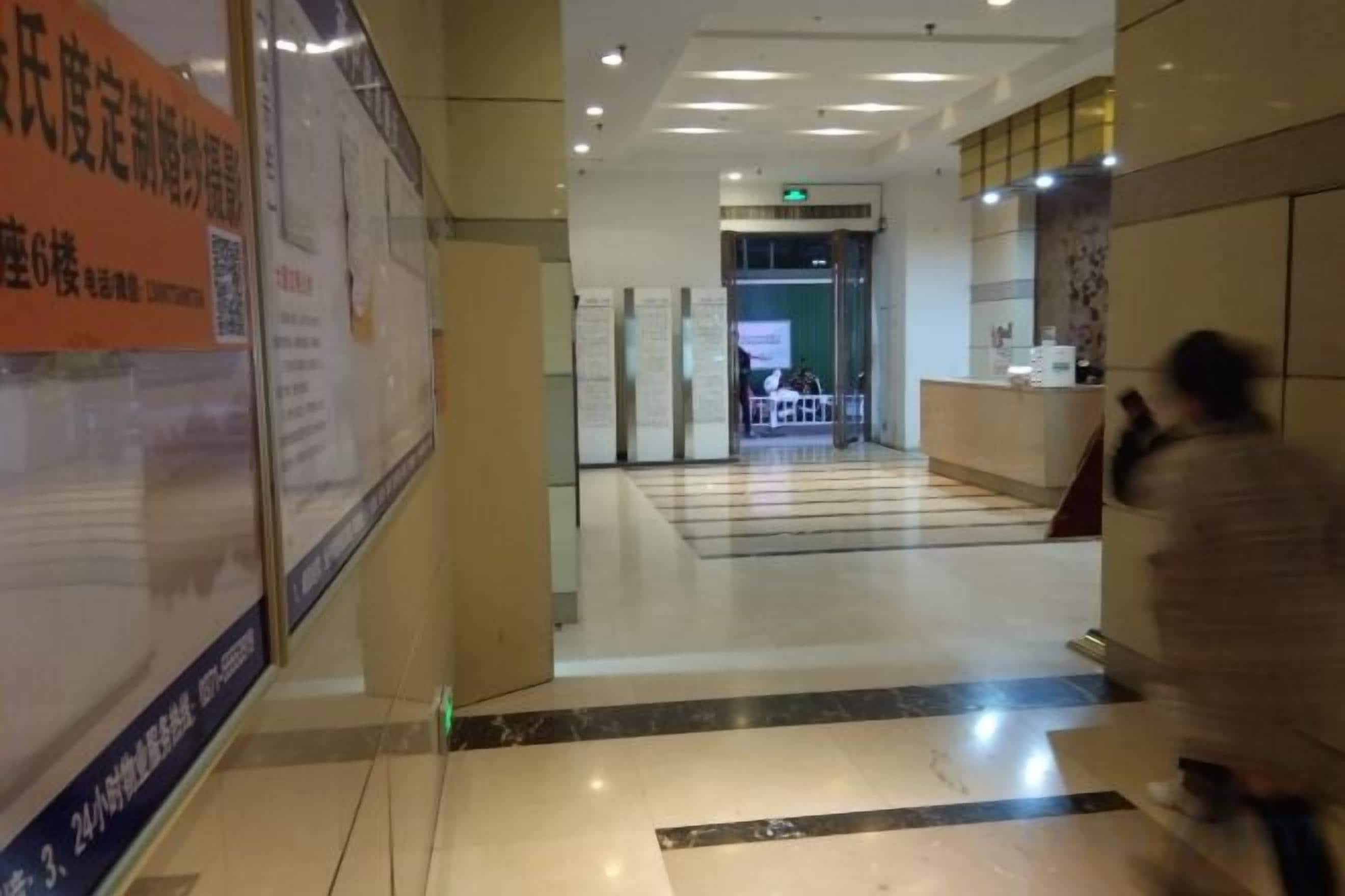Corredor de hotel com uma mesa de recepção, um cartaz na parede e piso revestido de azulejos.