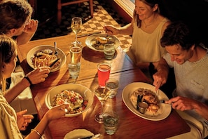 Um grupo de pessoas jantando em uma mesa de madeira, com diversos pratos, copos e talheres.
