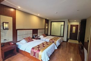 Quarto de hotel com duas camas, soalho de madeira, um espelho grande e uma porta.