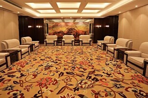 Sala de conferência com carpete estampado, mesas redondas e cadeiras dispostas para reuniões.